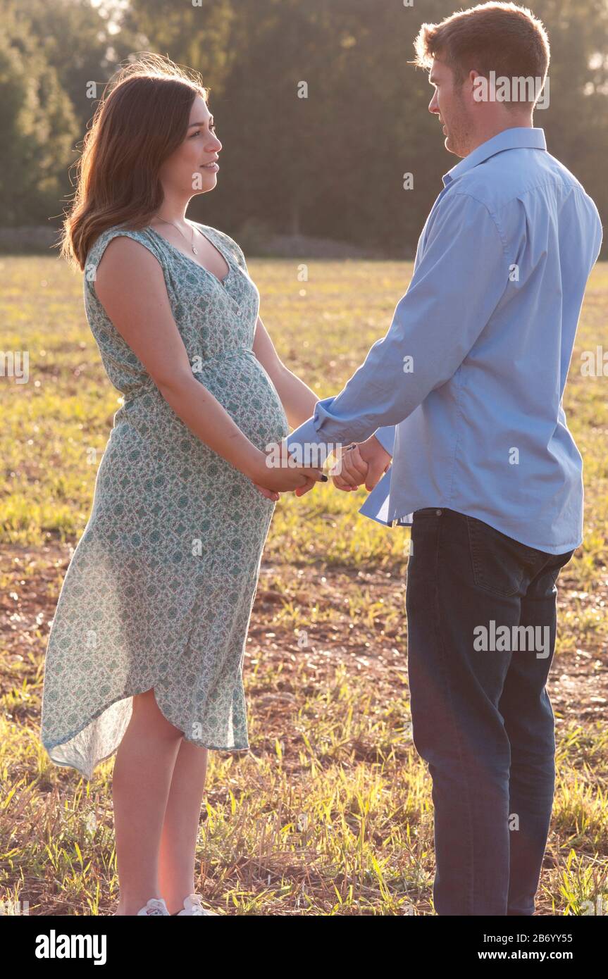 Pregnant young woman with her partner holding hands, looking at each ...