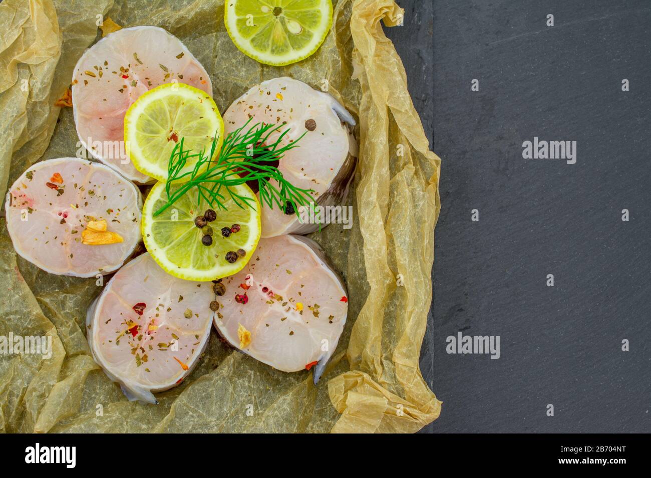 fresh fish fillets of conger eel ,lemon herbs , pepper, salt on black ...