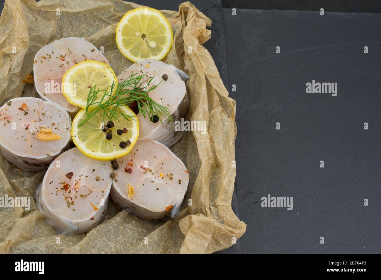 fresh fish fillets of conger eel ,lemon herbs , pepper, salt on black ...