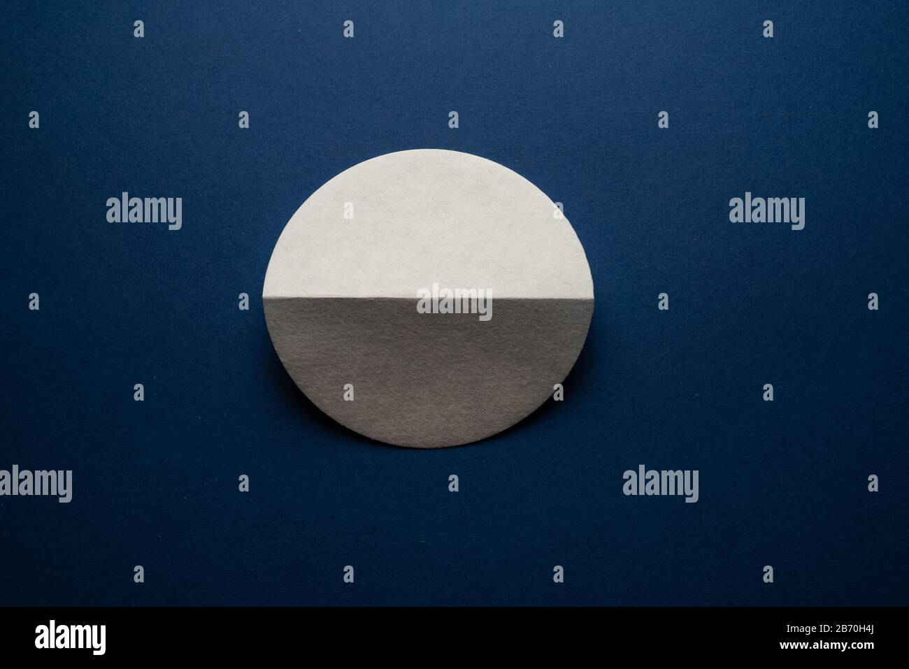 The paper circle is folded in half on dark blue. The light and dark ...