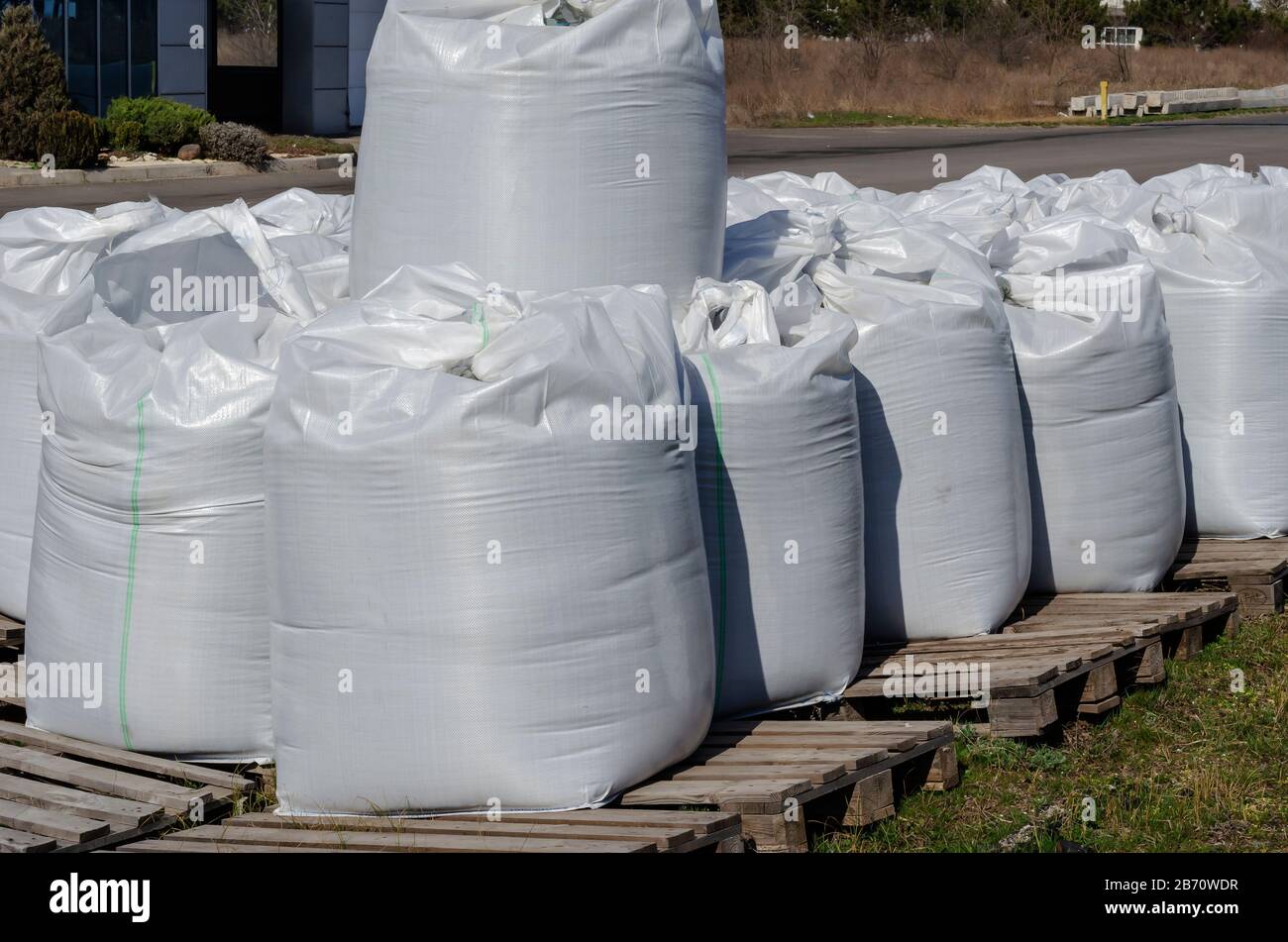 Bulk cargo in big bags. Full white big bags on wooden pallets outdoors ...