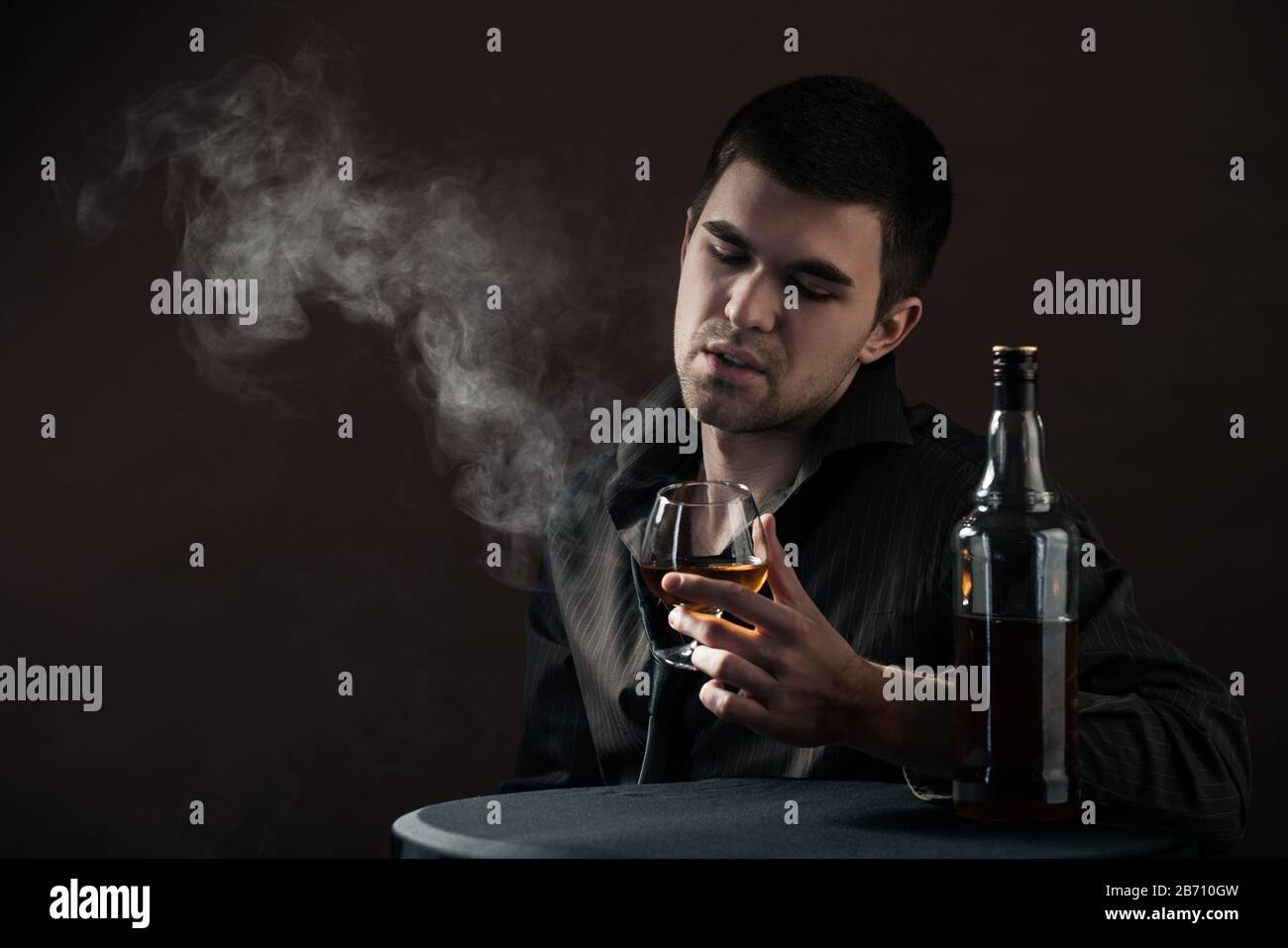 Sad young man beats an alcoholic drink from a chicken sitting in a dark ...