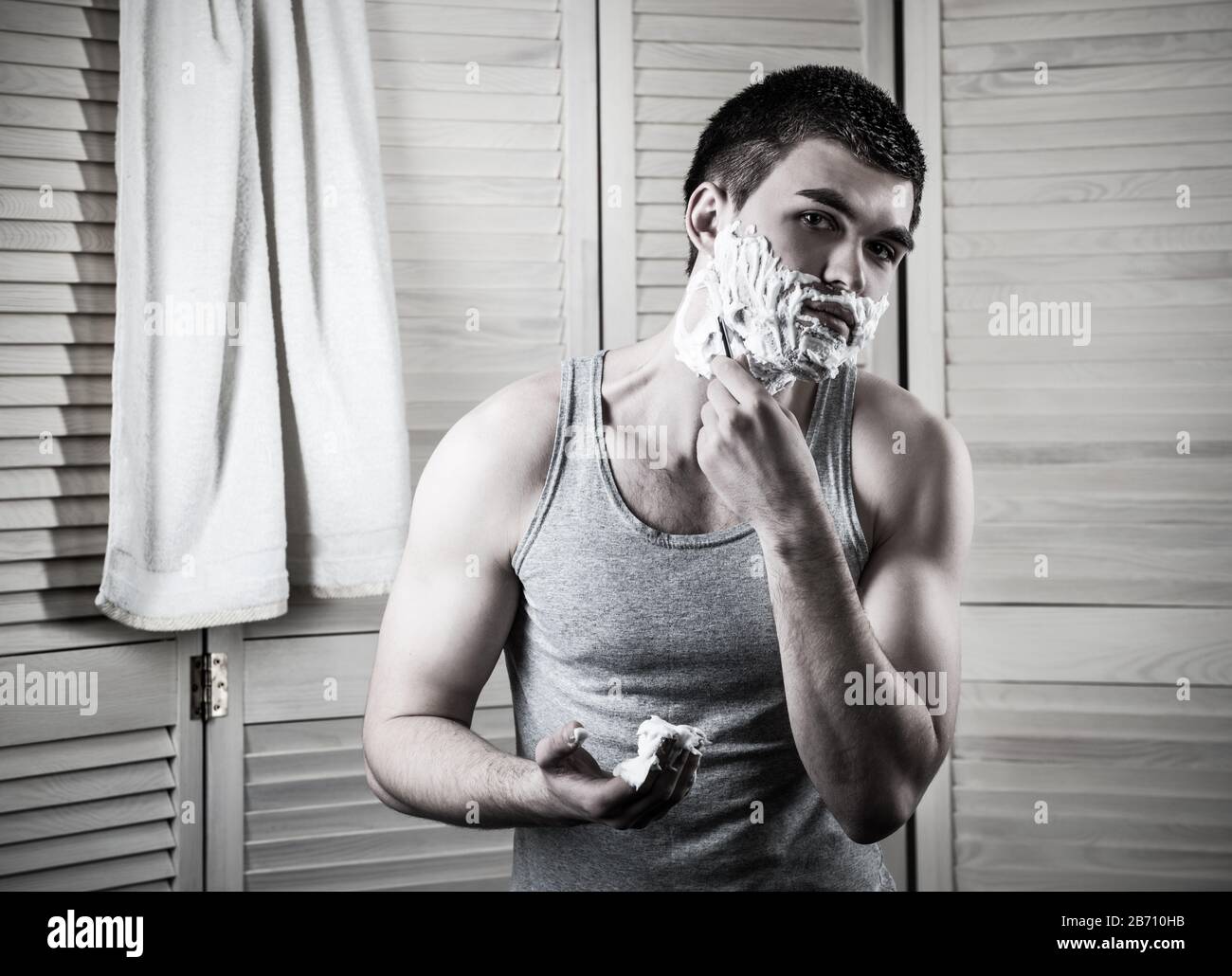 Portrait of a young man shaving his face in the bathroom during morning ...