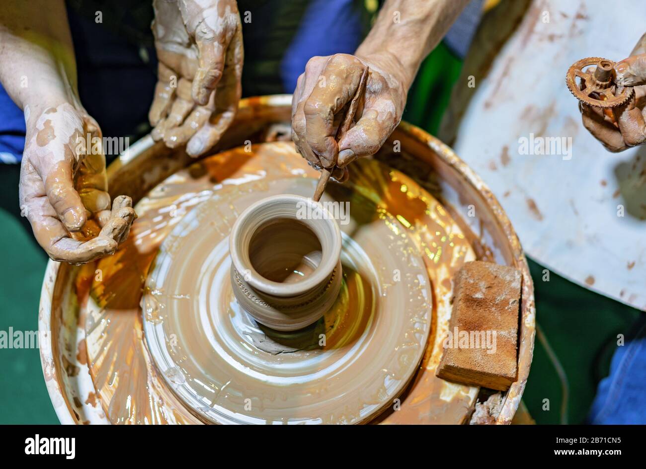 Professional potter makes a pot on a pottery wheel and teaches a pupil ...