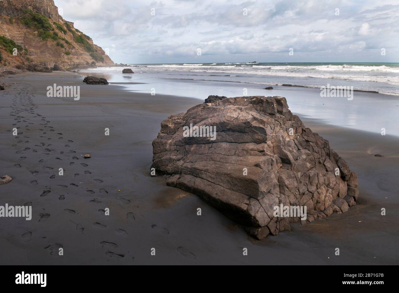Footsteps past a chunk of igneous rock at Muriwai beach, on New Zeaand ...