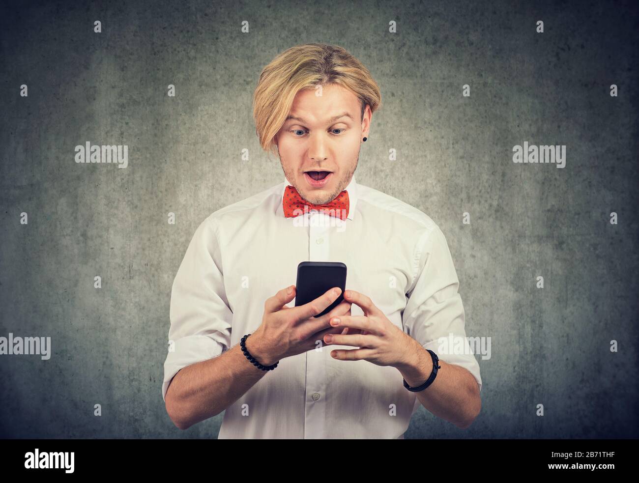 Man looking at his smart phone with an surprised expression on his face ...