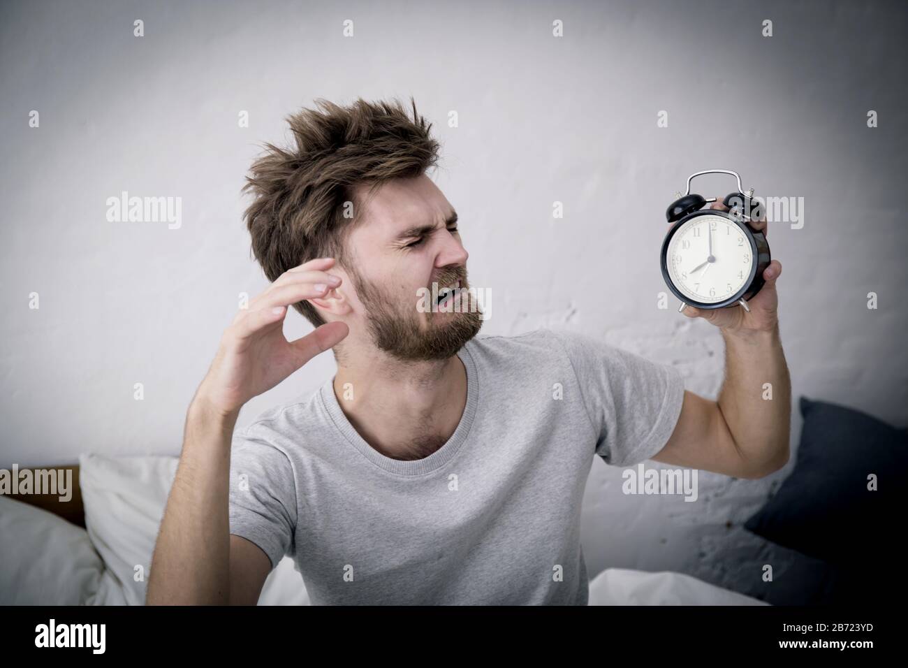 Portrait upset angry young man screaming at alarm clock on bedroom ...