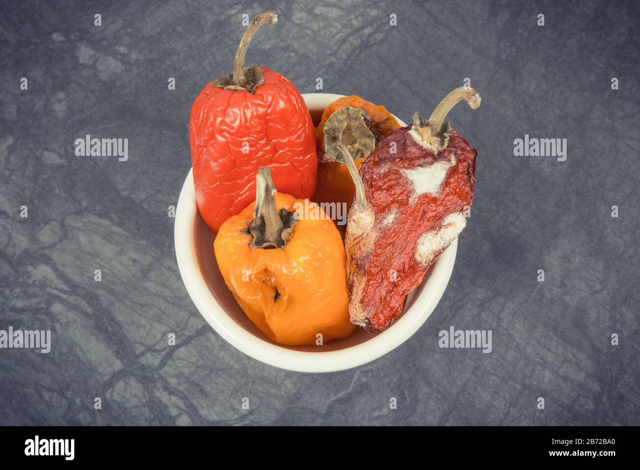 Old wrinkled moldy peppers in white bowl on dark background, concept of ...