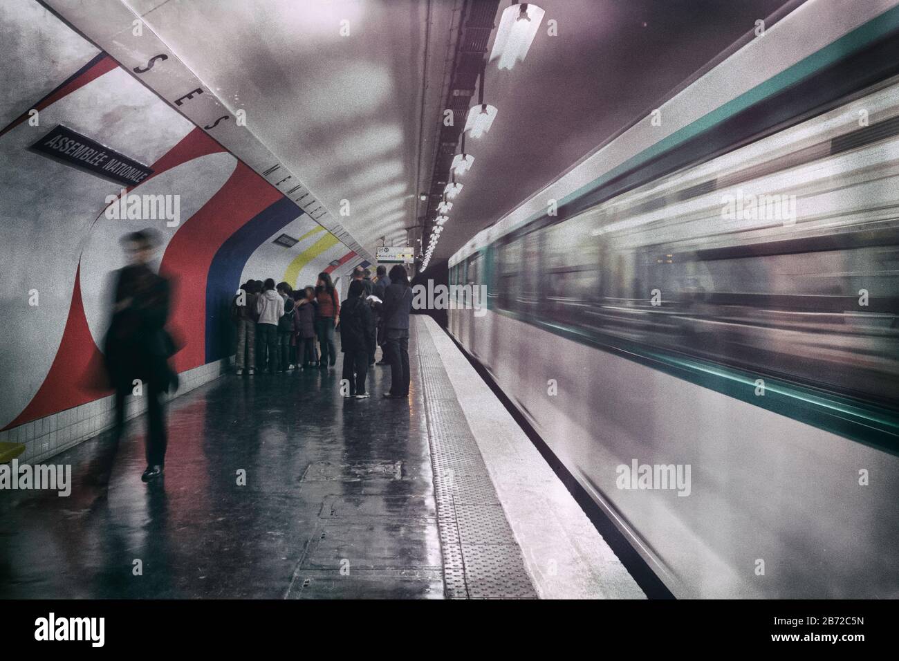 A departing train in motion as passengers walk toward the platform exit ...