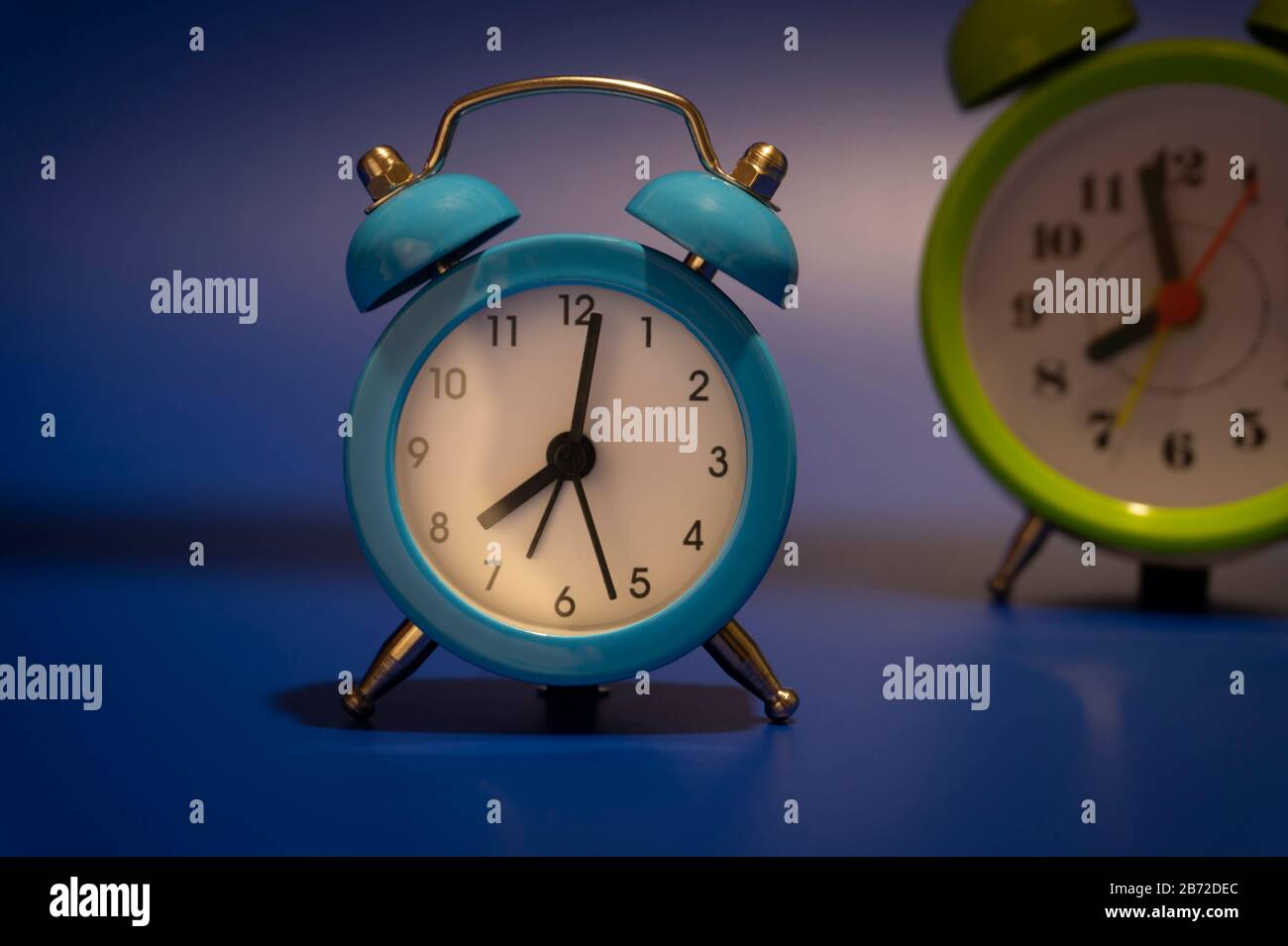 Blue and yellow twin bell analog alarm clocks over a glowing blue ...