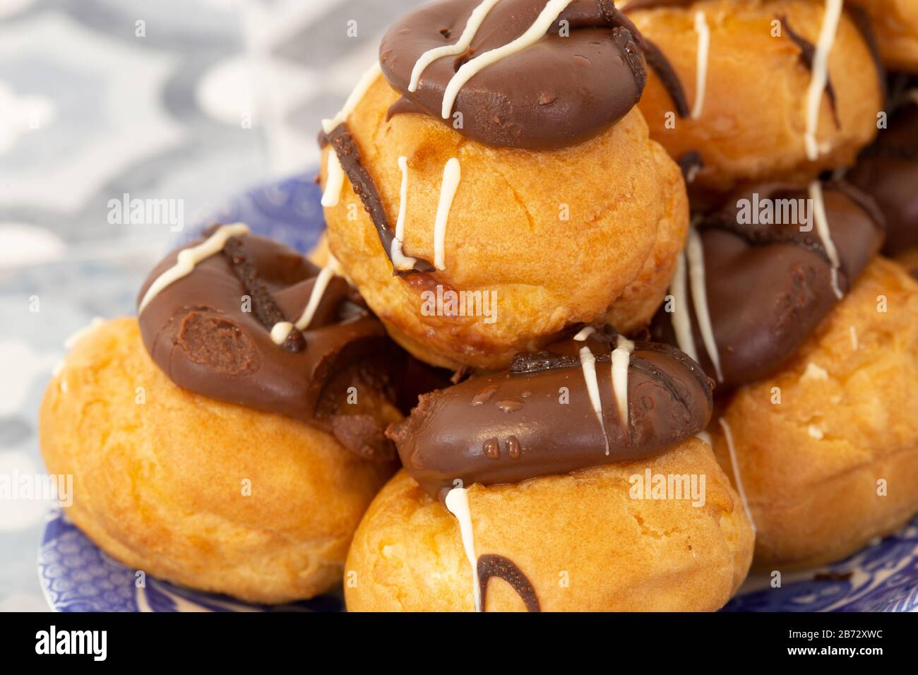 Profiteroles, coated in chocolate, stacked on a pattermed blue and ...