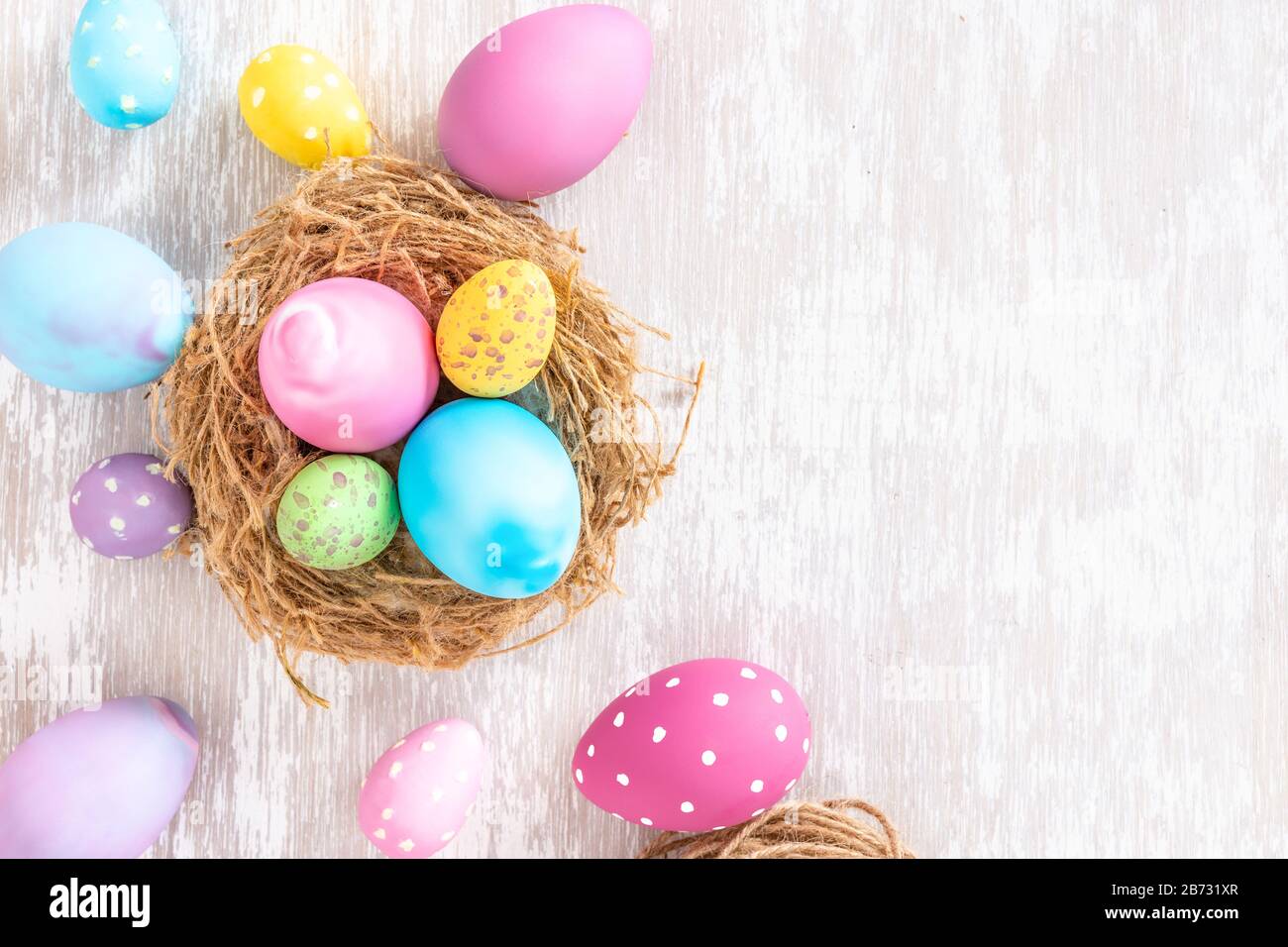 Easter eggs in nest and scattered over simple white wash wood tabletop ...