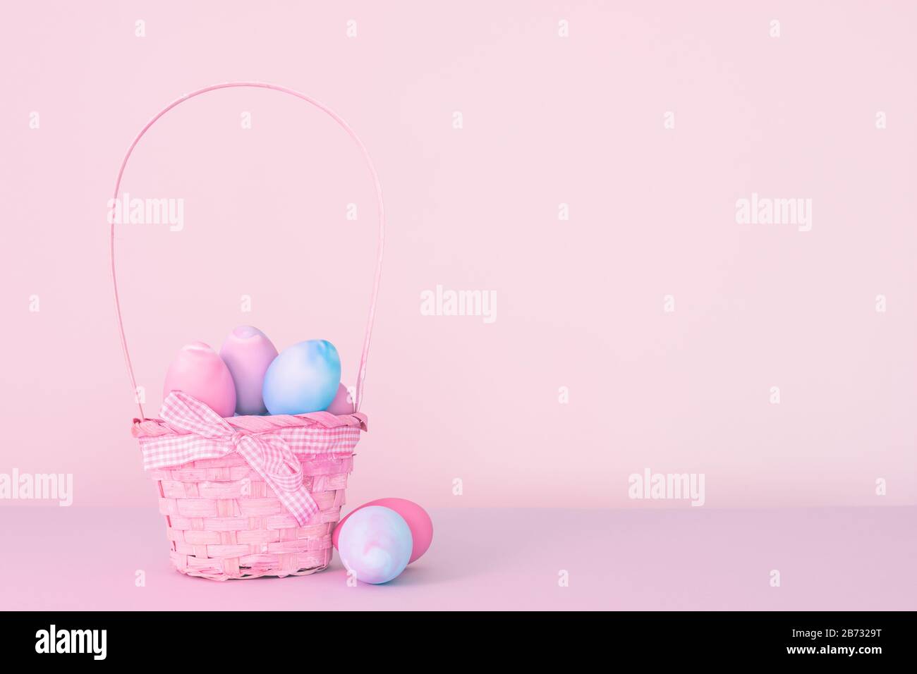 Pastel pink and blue Easter eggs in a weaved basket with a pink ...