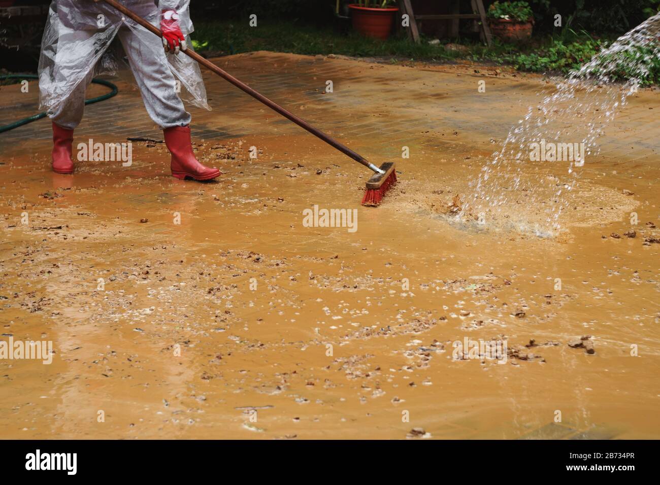 Woman (only legs visible) in red rubber boots cleaning stone pavement ...