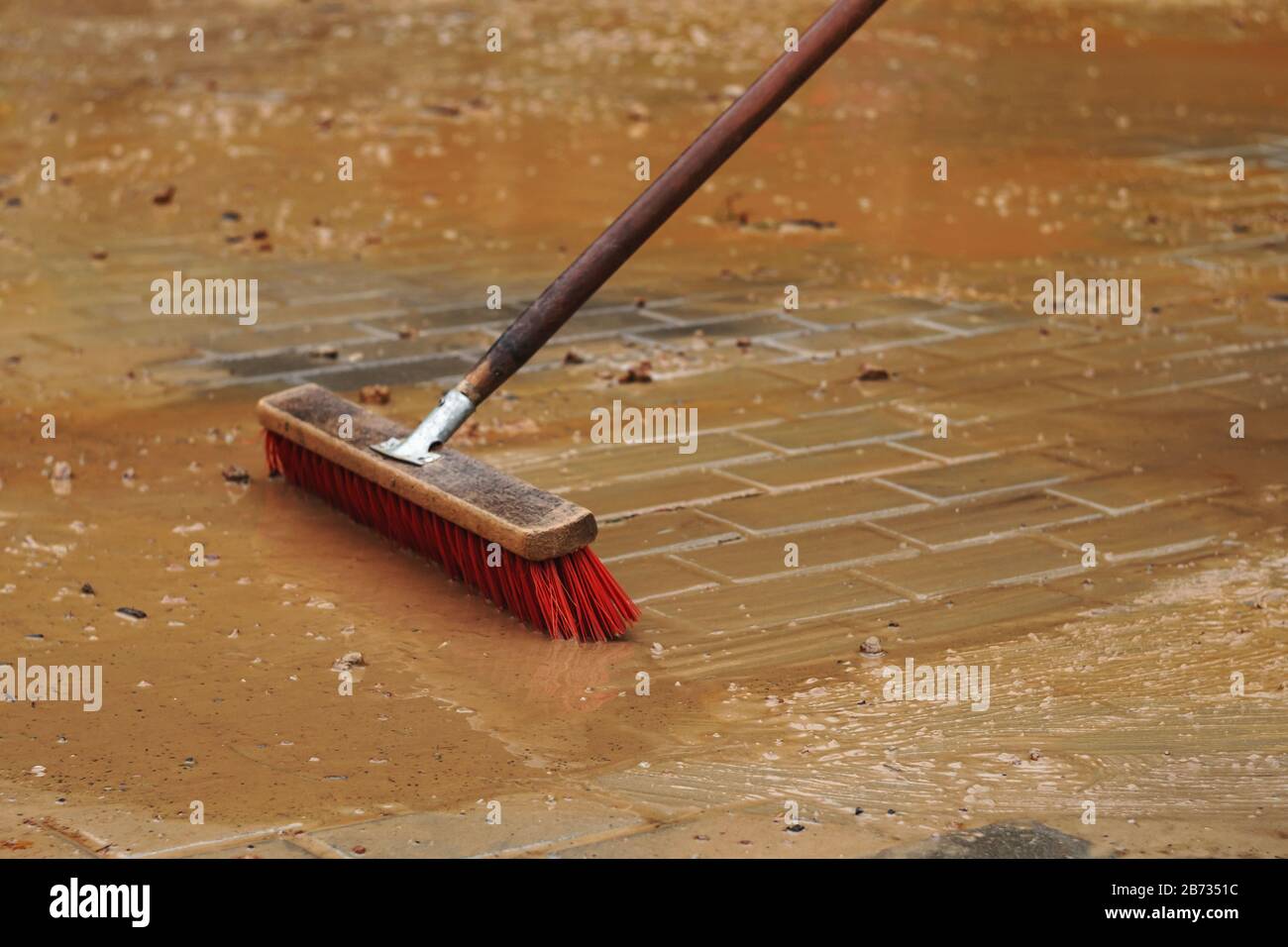 Red plastic rough bristled brush cleaning sand and water covered stone ...