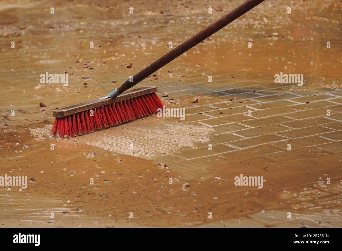 Red plastic rough bristled brush cleaning sand and water covered stone ...