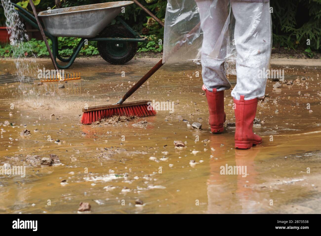 Woman (only legs visible) in red rubber boots cleaning stone pavement ...