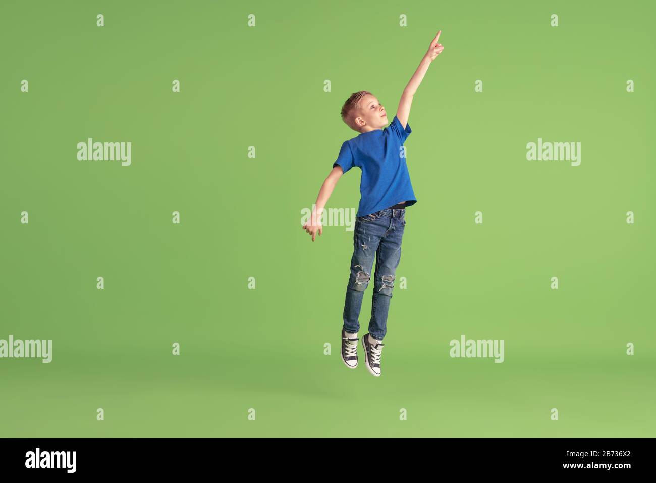 Pointing. Happy boy playing and having fun on green studio background ...