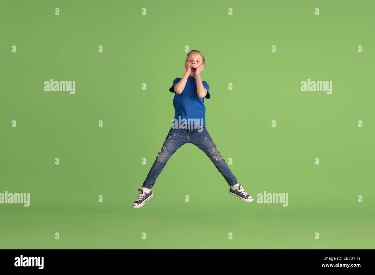 Astonished. Happy boy playing and having fun on green studio background ...