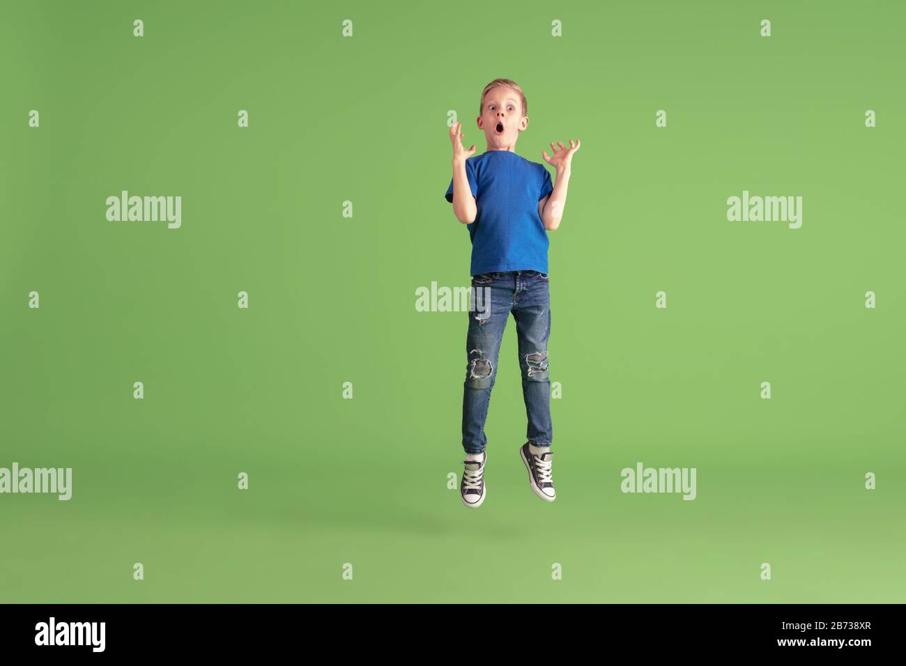 Shocked. Happy boy playing and having fun on green studio background ...