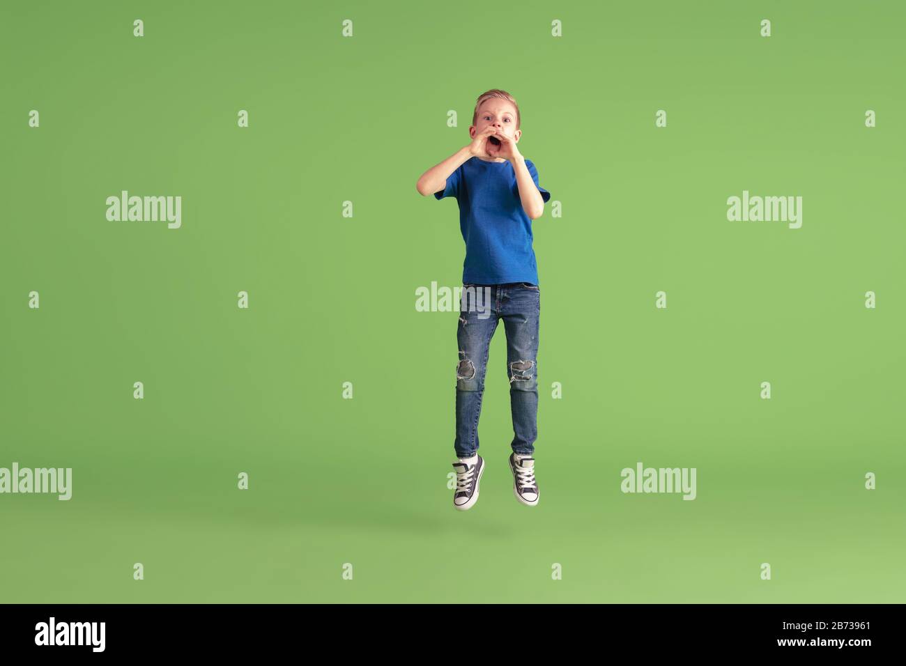 Shouting. Happy boy playing and having fun on green studio background ...