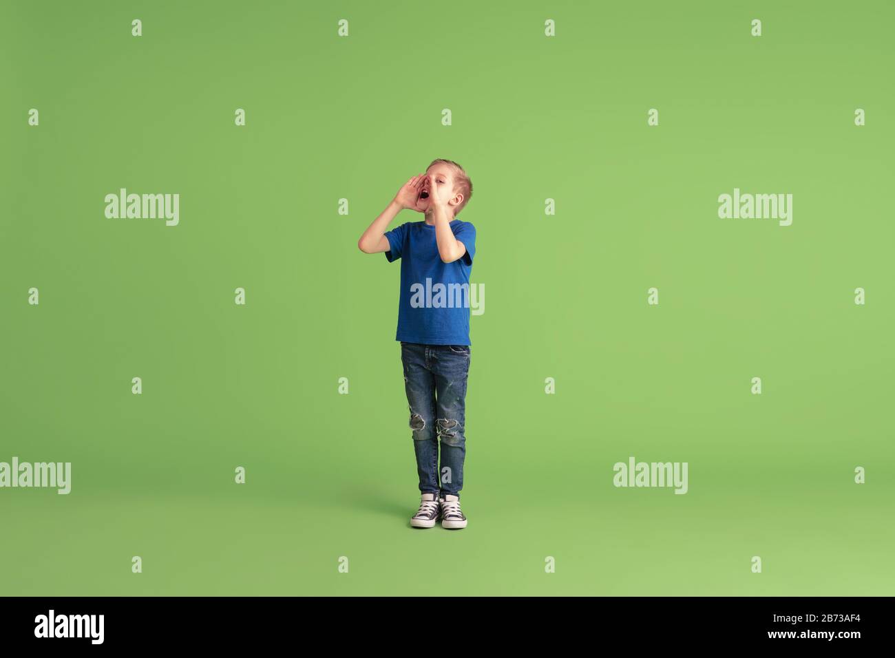 Shouting. Happy boy playing and having fun on green studio background ...