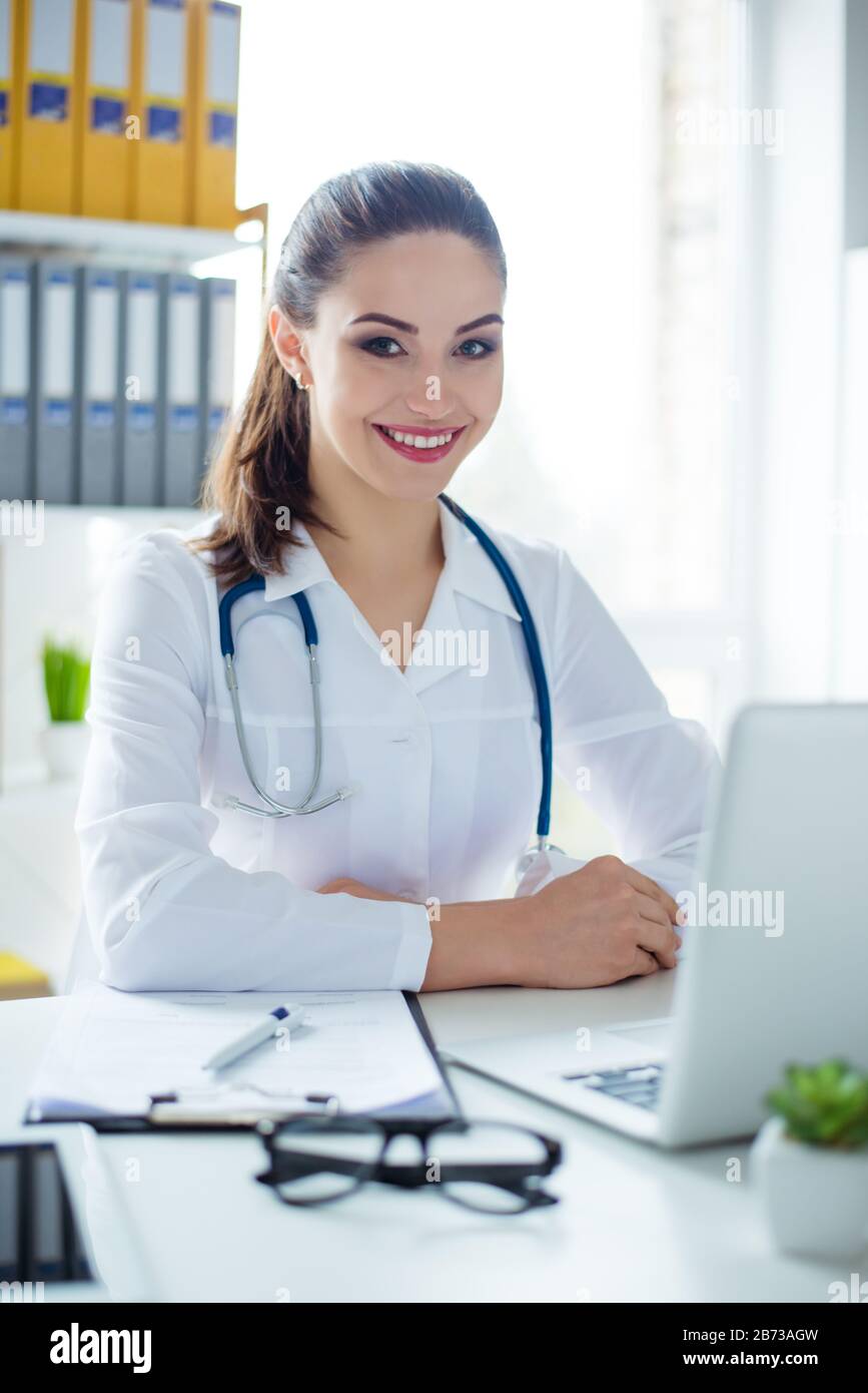 Vertical portrait of smiling doctor in uniform sitting at the table in ...