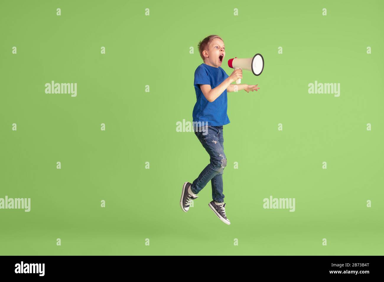 Shouting, calling. Happy boy playing and having fun on green studio ...