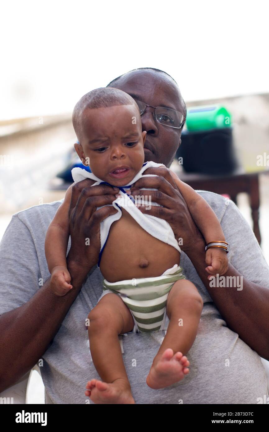a young man in glasses and gray tee-shirt rocking his baby while he ...