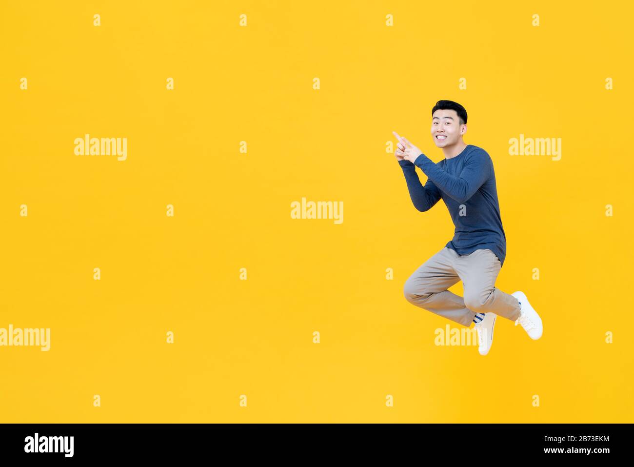 Young happy Asian man floating in mid-air pointing two fingers at blank ...