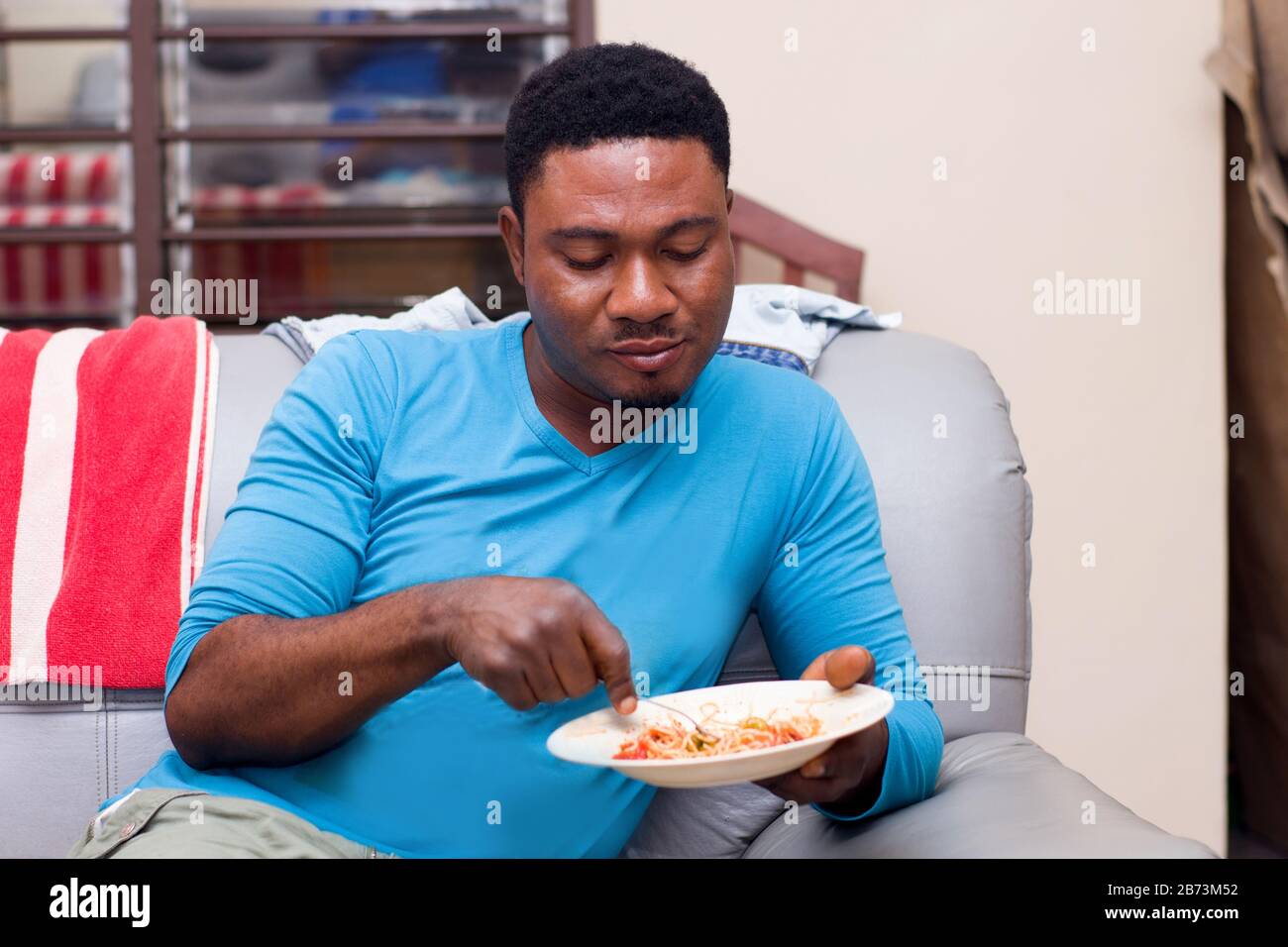 young man sitting in an armchair eating spaghetti holding a plate in ...