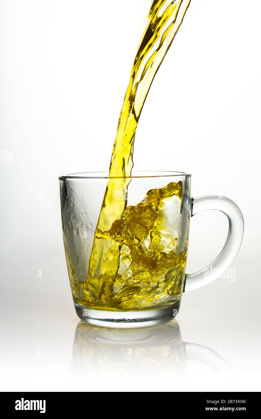 Splash of yellow tea in a transparent cup, pouring a transparent jet of ...