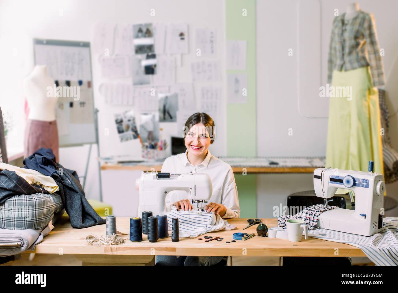 Beautiful seamstress sewing at her workshop. Dressmaker working on the ...
