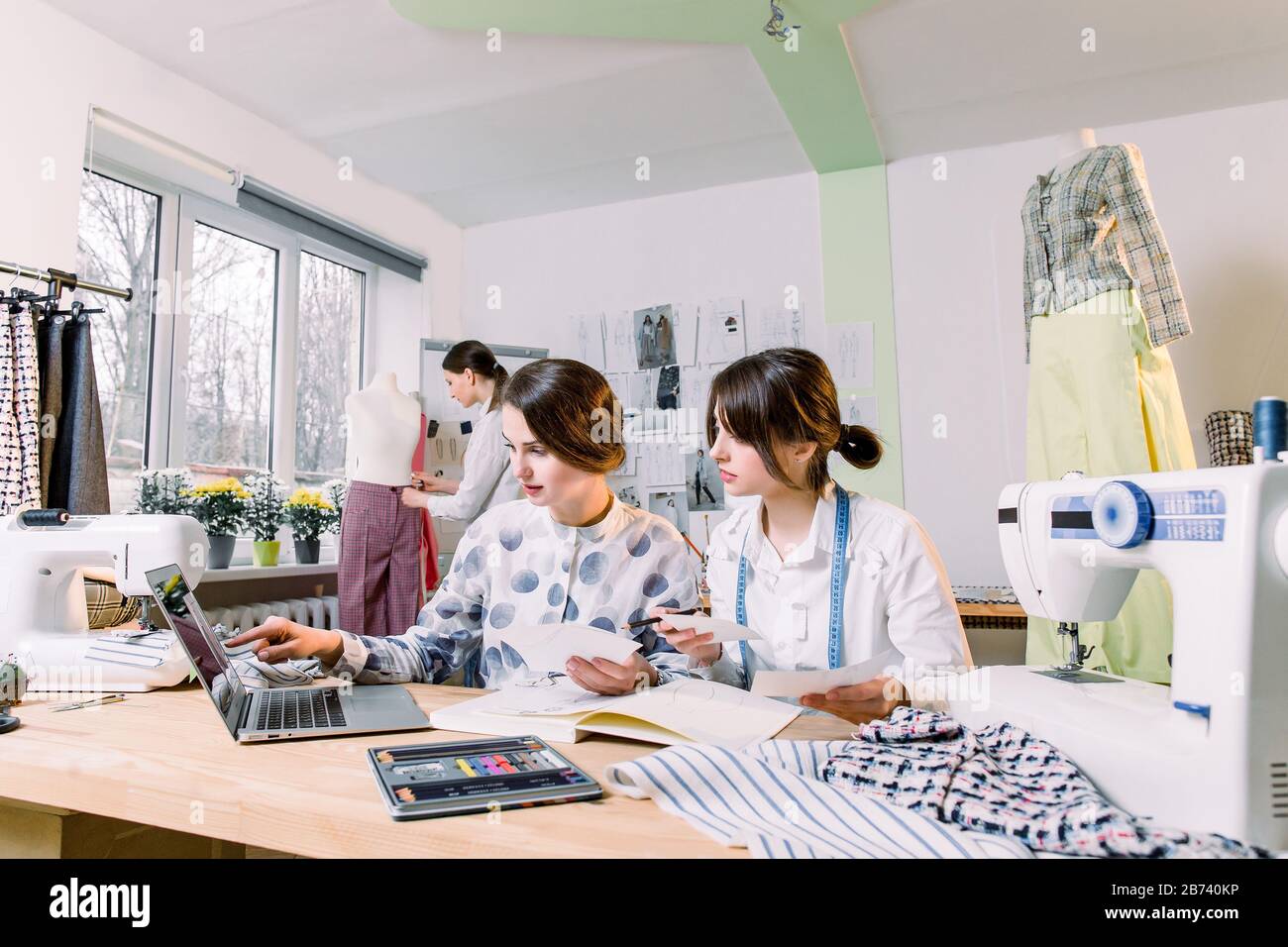 Two attractive women dressmakers designers choosing trendy sketches and ...