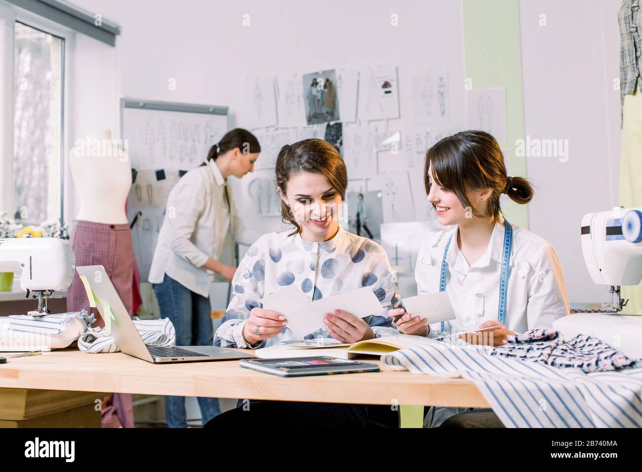 Two attractive women dressmakers designers choosing trendy sketches and ...