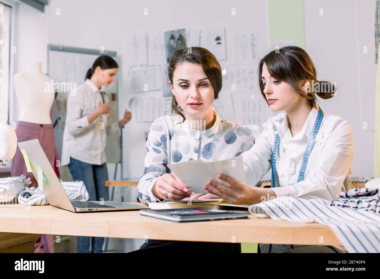 Two attractive women dressmakers designers choosing trendy sketches and ...