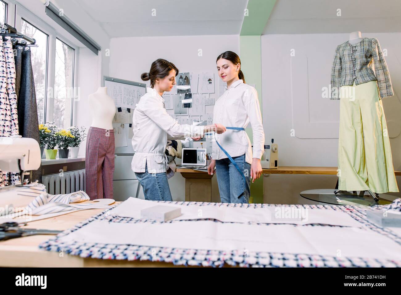 Pretty young female tailor measuring her client woman to make stylish ...