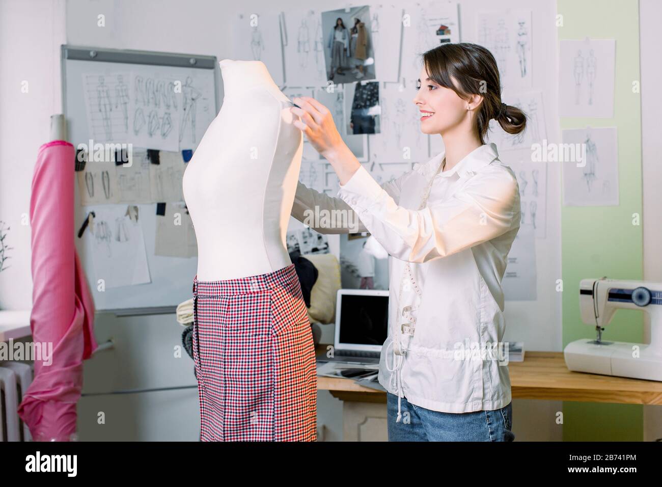 Female dressmaker working on new model tailoring pants on mannequin in ...