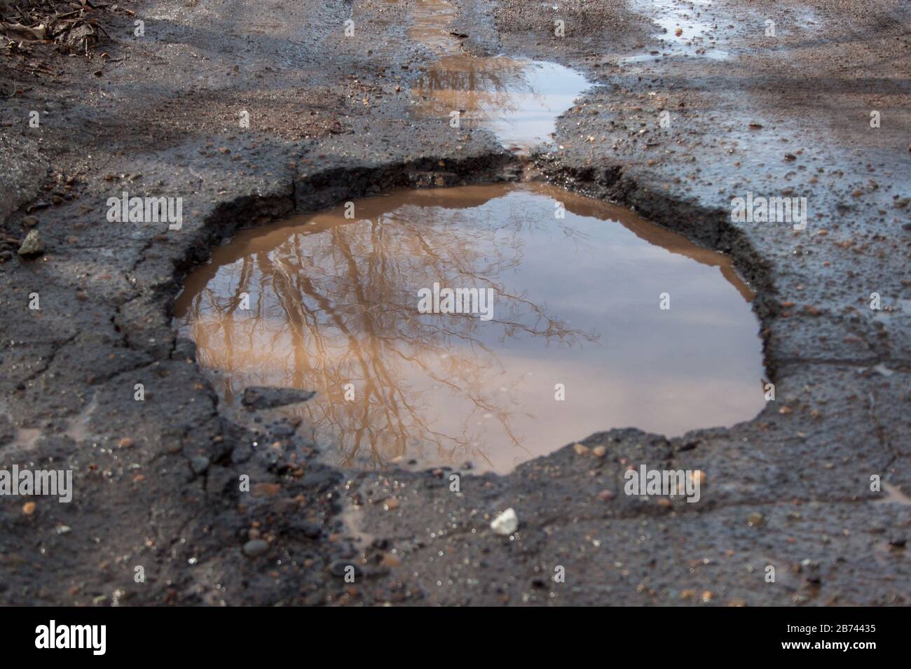 The bad asphalted road with a pothole filled with water. Dangerous ...