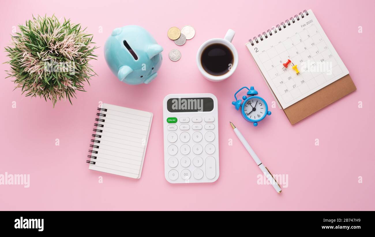 Piggy bank, calculator, calendar, clock and coffee cup on pink desk ...