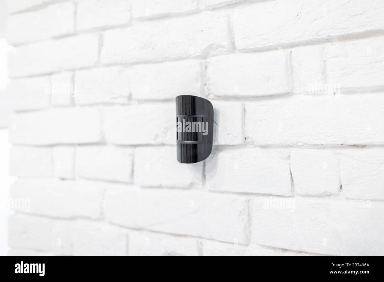 Black wireless motion sensor of alarm system mounted on the white brick ...