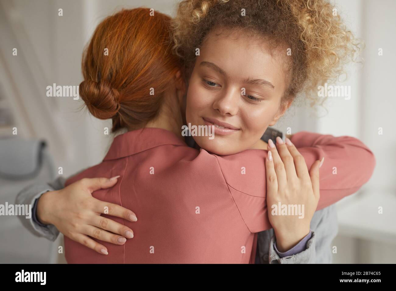 Beautiful young woman giving a friendly hug to her friend during their ...