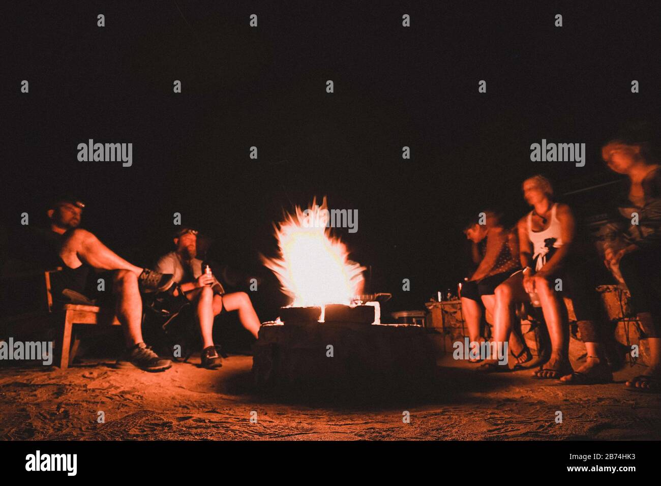 Low angle of a group of friends sitting around a bonfire at night and ...