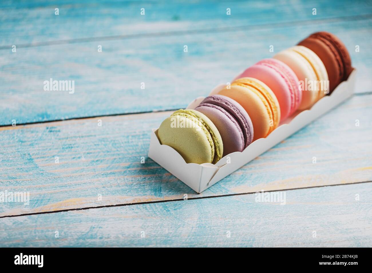 Macaroni cookies of different colors in a box on a blue, old wooden ...
