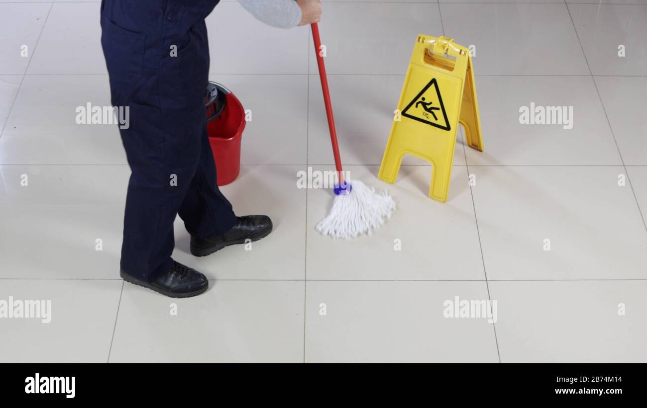 Man cleaner cleaning the floor and a caution sign wet floor Stock Photo ...