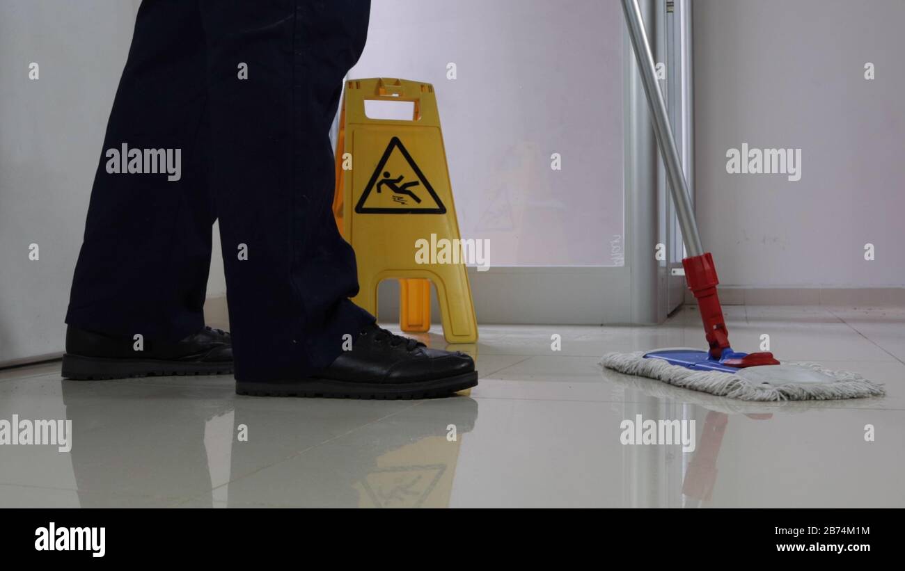 Man cleaner cleaning the floor and a caution sign wet floor Stock Photo ...