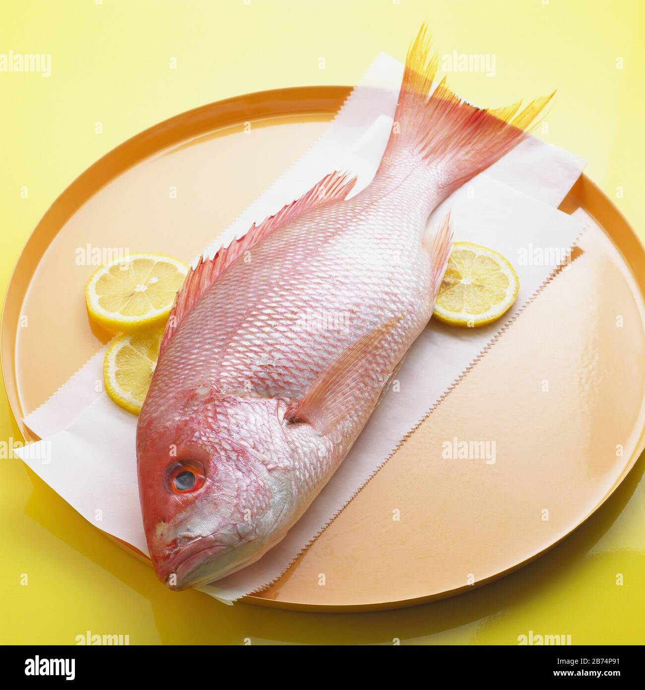 Whole red snapper fish on a yellow plate with lemons on the side Stock ...