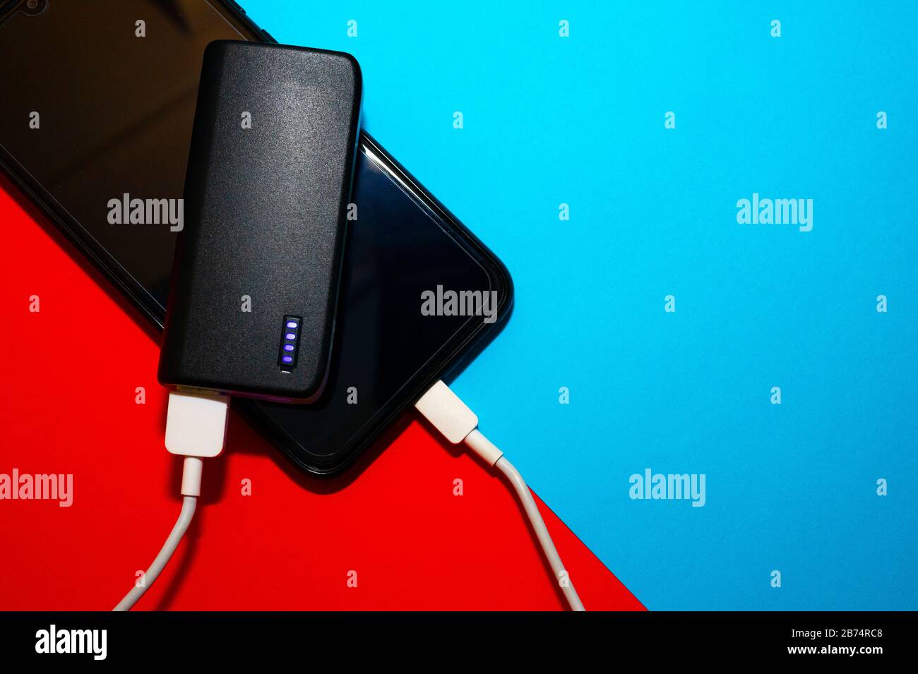 Powerbank loading a cell phone on a blue and red background. Powerbank ...
