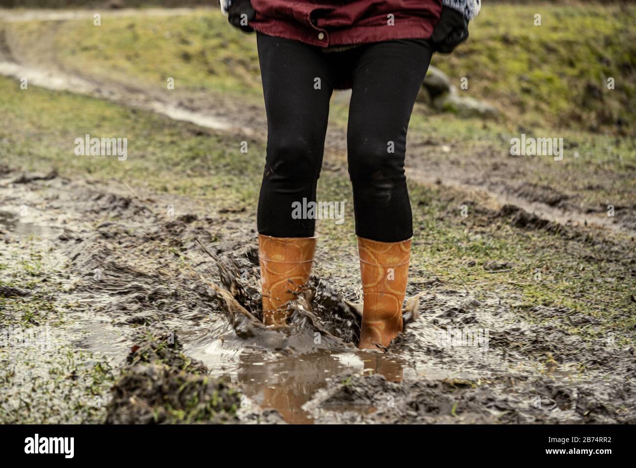 woman jumping in the puddle of mud in autumn with orange rubber boots ...