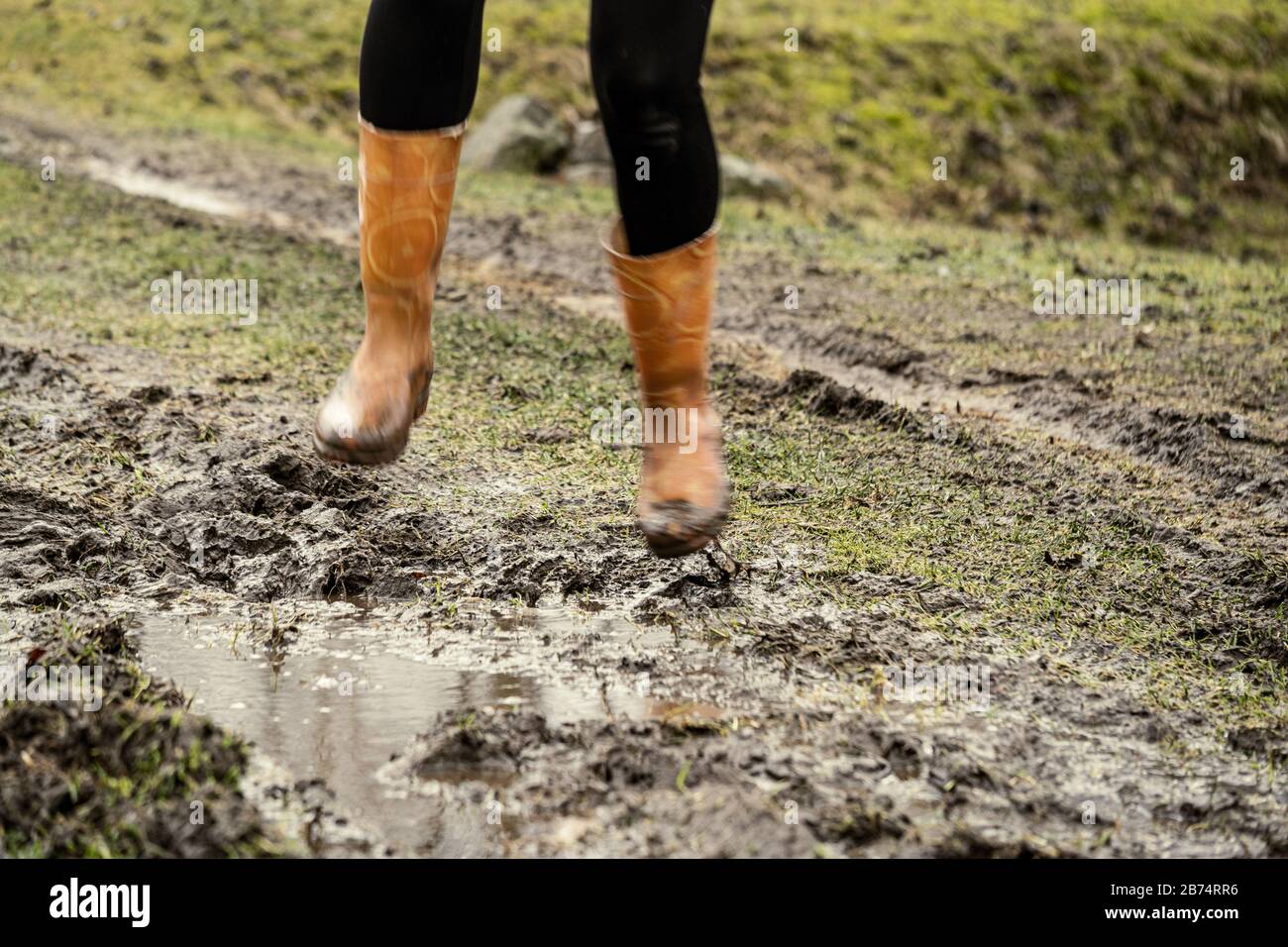woman jumping in the puddle of mud in autumn with orange rubber boots ...